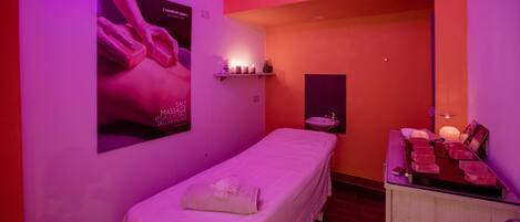 Um quarto de spa com uma mesa de massagem, uma prateleira com velas e uma pia.