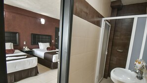 Quarto de hotel com duas camas, banheiro com pia e chuveiro.