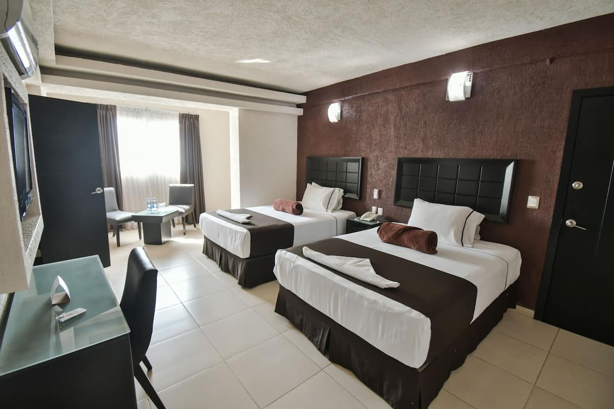 Quarto de hotel com duas camas, uma escrivaninha, uma cadeira, uma televisão e uma janela com cortinas.