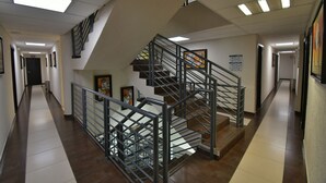 Interior moderno com uma escada central, um corredor com quadros e um teto com iluminação embutida.