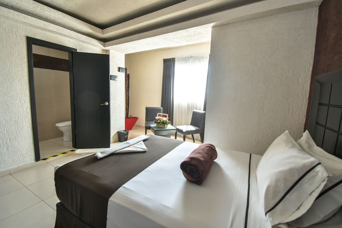 Quarto de hotel com cama, poltrona, mesinha com um vaso de flores e vista para o exterior.