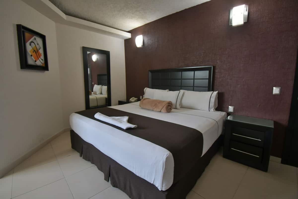 Quarto de hotel com uma cama grande, uma mesa de cabeceira, um espelho e um quadro na parede.