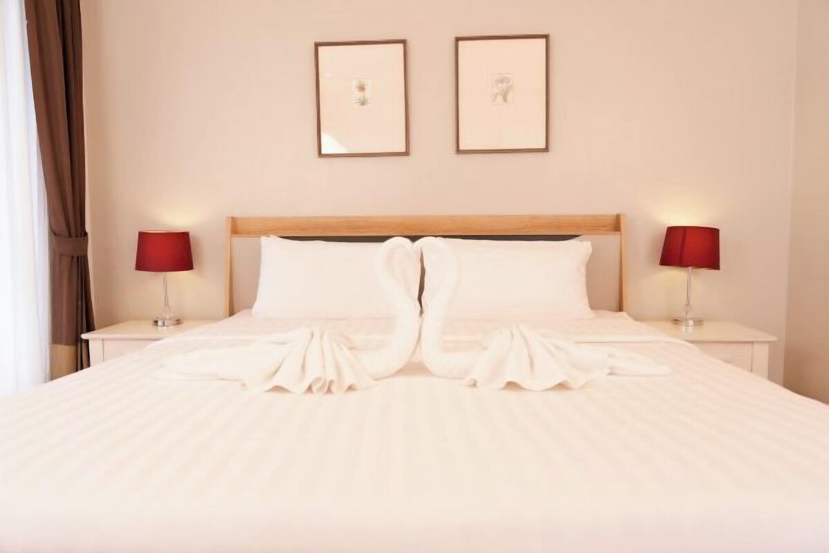Quarto de hotel com uma cama grande, duas mesas de cabeceira com luminárias e duas molduras na parede.