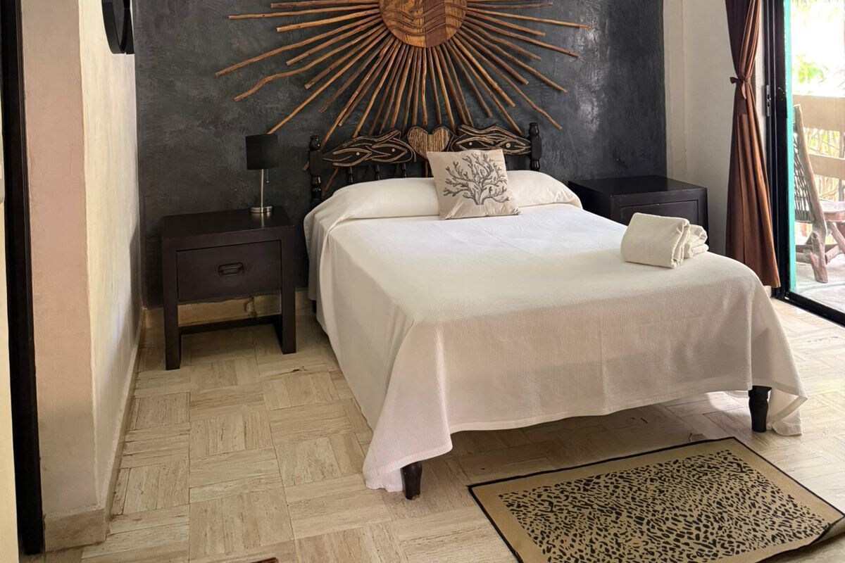 Quarto com cama, mesas de cabeceira, uma obra de arte na parede e vista pela janela.
