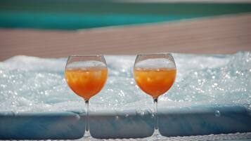 Dois copos de bebida de laranja sobre uma mesa à beira da piscina, com a piscina ao fundo.