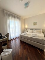 Quarto de hotel com cama, escrivaninha, cadeira e janela com cortinas.