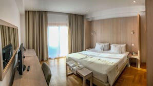 Quarto de hotel com uma cama grande, uma escrivaninha com cadeira, televisão e abajur.