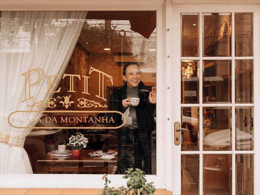 Entrada de hotel com um letreiro indicando 'PETIT CASA DA MONTANHA' e uma pessoa parada na porta.