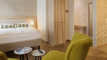 Quarto de hotel com uma cama, uma mesinha com um controle remoto e uma poltrona verde.