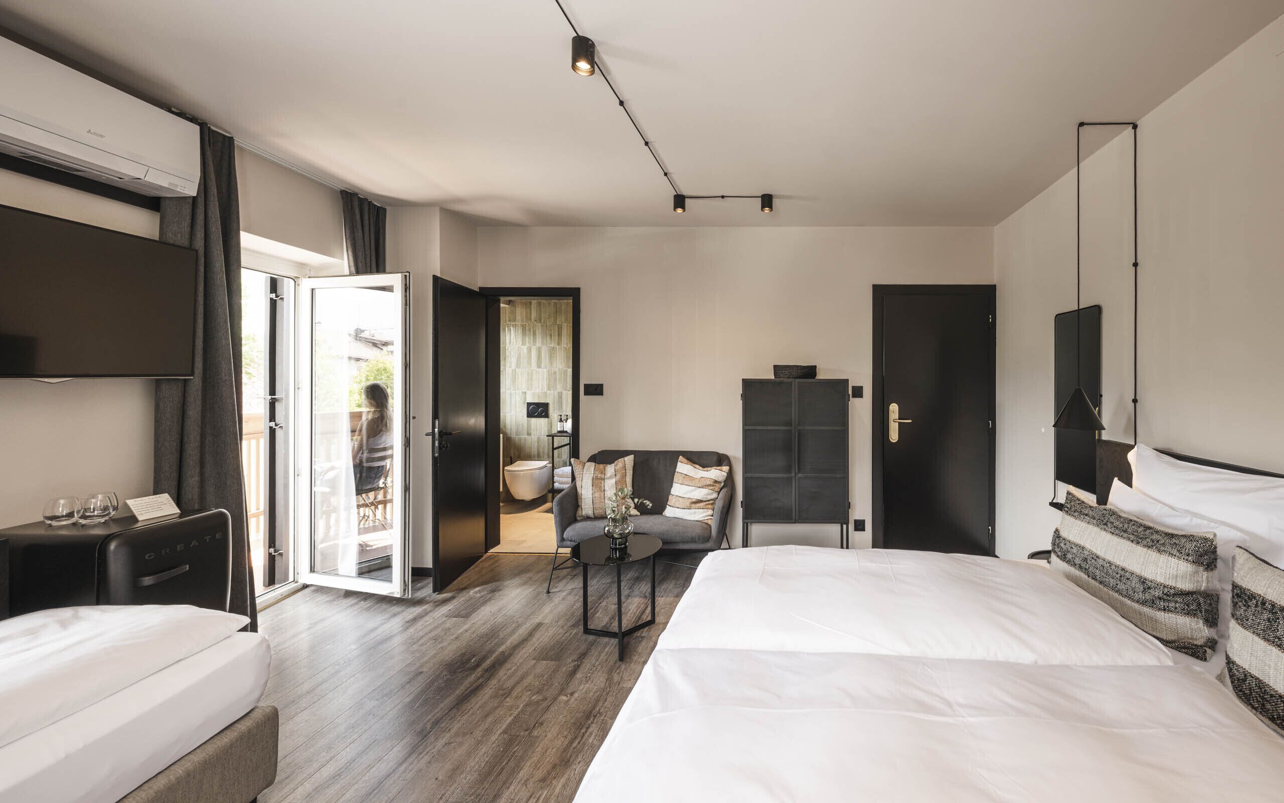 Quarto de hotel moderno com uma cama grande, uma mesa, uma cadeira, uma TV e um banheiro visível por uma porta aberta.