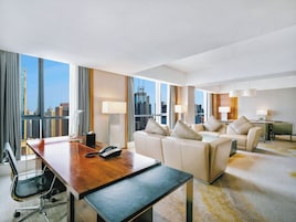 Quarto de hotel com uma secretária grande, um sofá e vista para a cidade.