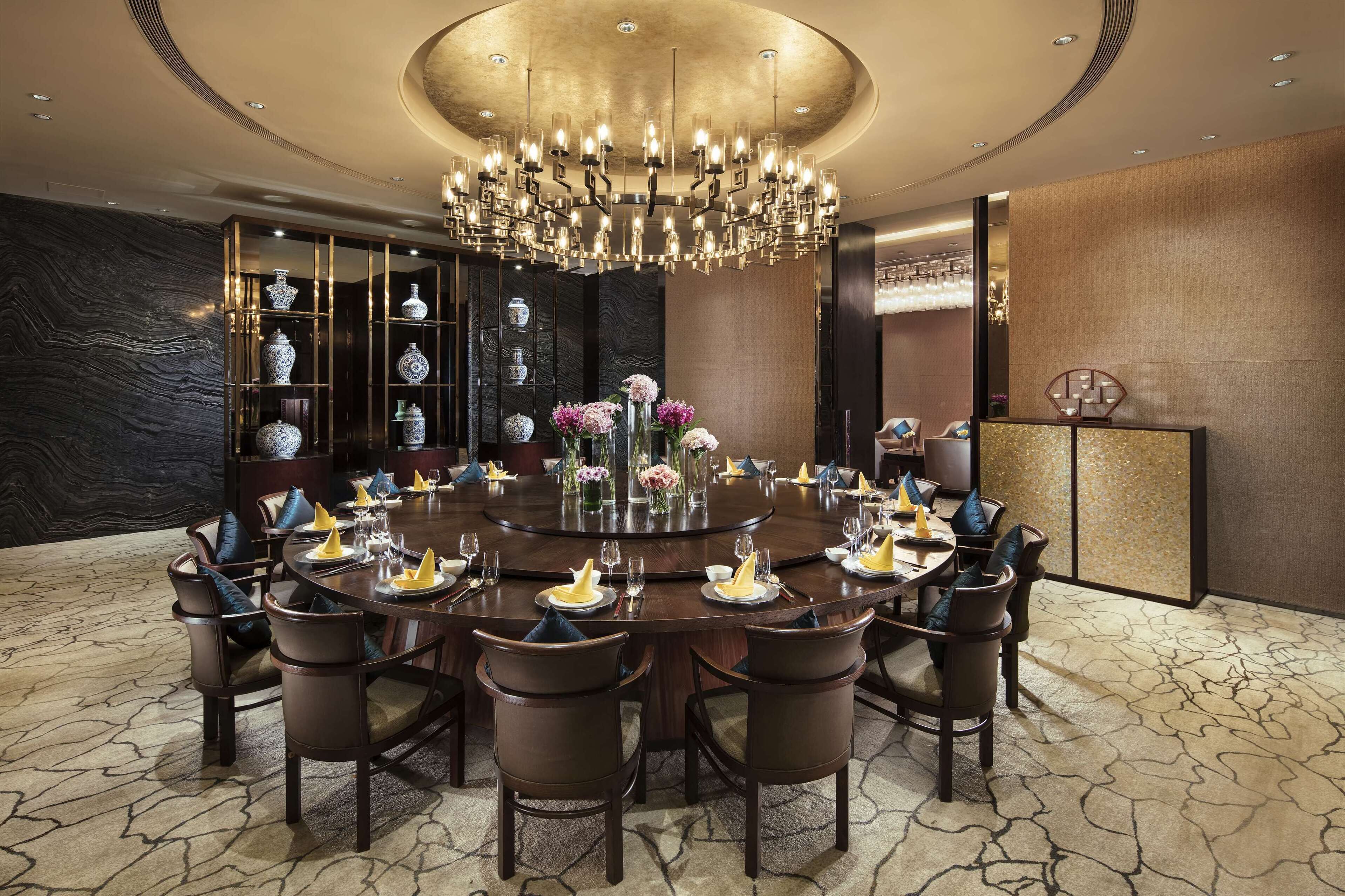 Uma mesa de jantar redonda com várias cadeiras, um candelabro e uma exposição de vasos e flores.