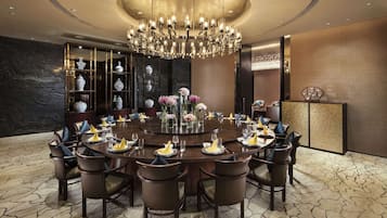 Uma mesa de jantar redonda com várias cadeiras, um candelabro e uma exposição de vasos e flores.