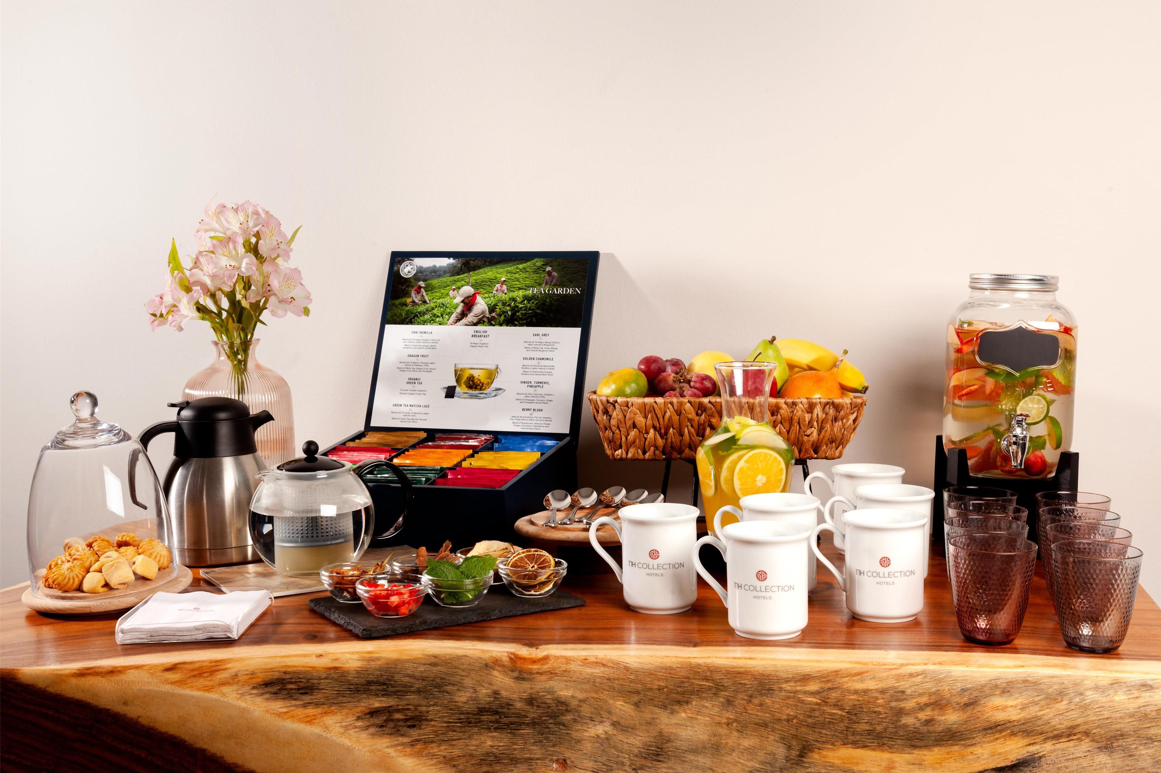 Disposição para café da manhã com cafeteira, bule, chá, pães, frutas e xícaras de café.