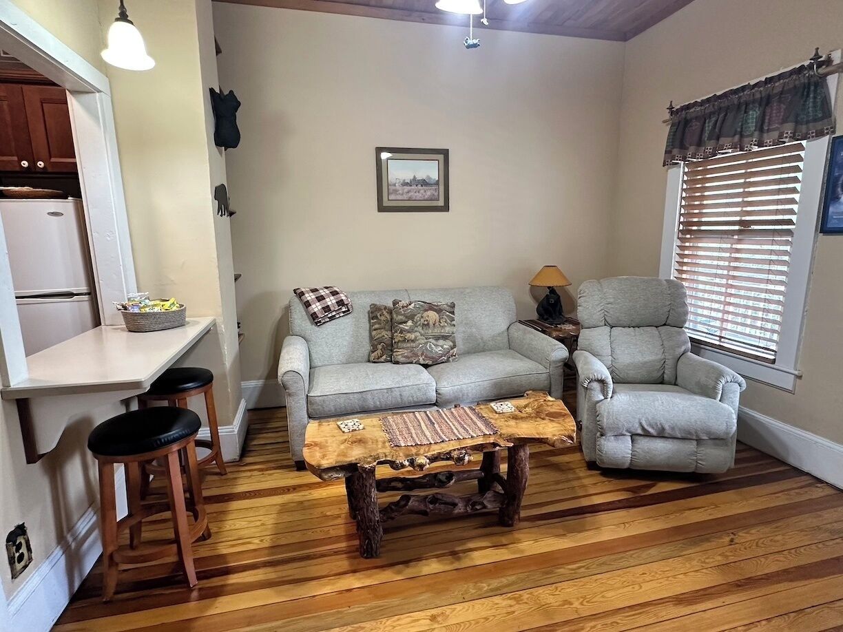 Sala de estar com sofá, duas poltronas, mesa de centro e cozinha com bancada e banquetas.