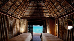 Quarto com telhado de colmo, duas camas, um deck de madeira e vista para o mar.