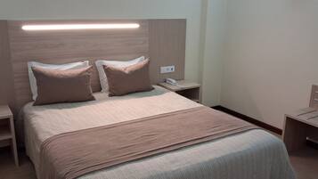 Quarto de hotel com cama, mesas de cabeceira, abajur e telefone.