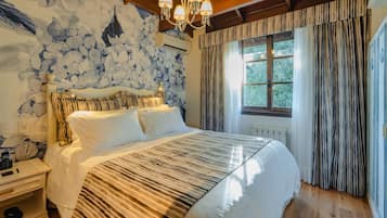 Quarto com cama grande, roupa de cama listrada, parede florida, janela com cortinas e lustre.