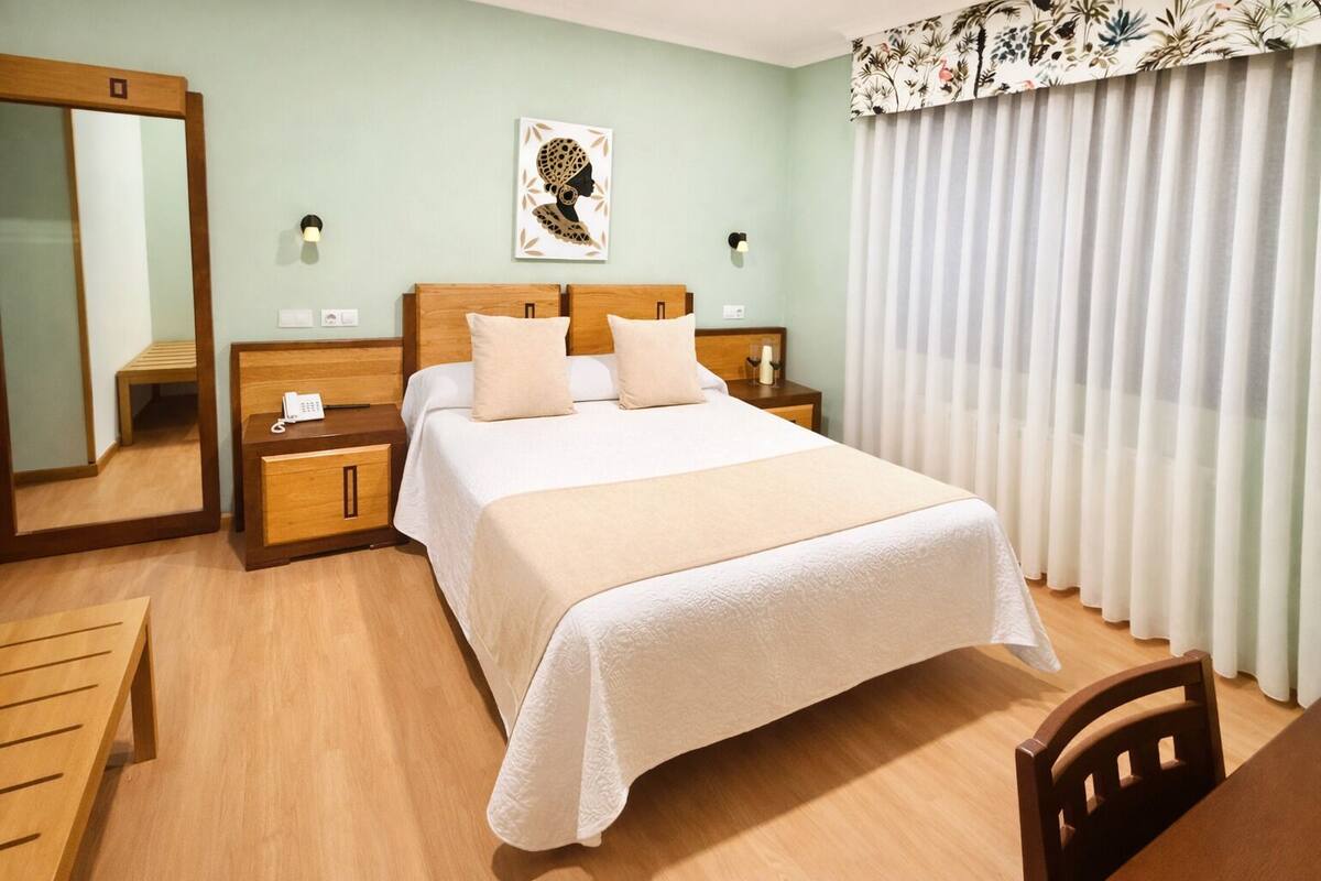 Quarto de hotel com cama, mesas de cabeceira, espelho, escrivaninha e cadeira.