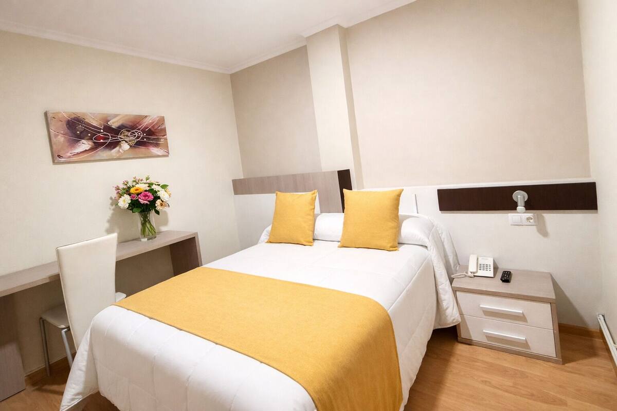Quarto de hotel com cama, mesa de cabeceira, cadeira e um quadro na parede.