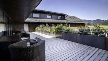 Um deck moderno ao ar livre com móveis de vime, vista para um edifício tradicional e um jardim paisagístico.