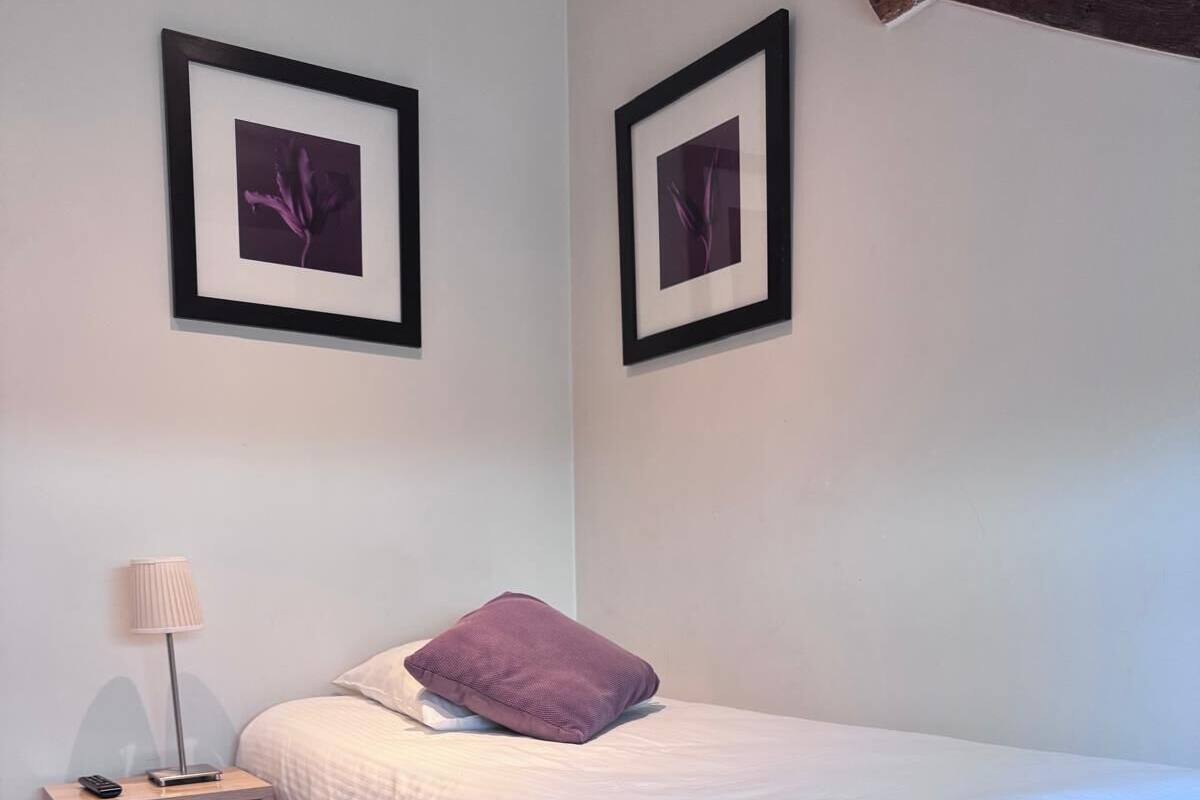 Quarto com cama, mesa de cabeceira, abajur e duas quadros na parede.