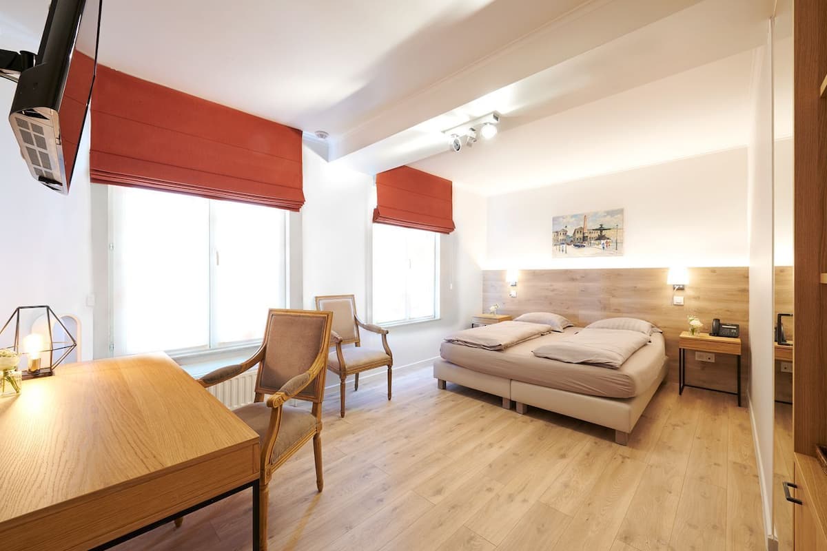 Quarto com cama, duas cadeiras, uma mesa e um quadro na parede.