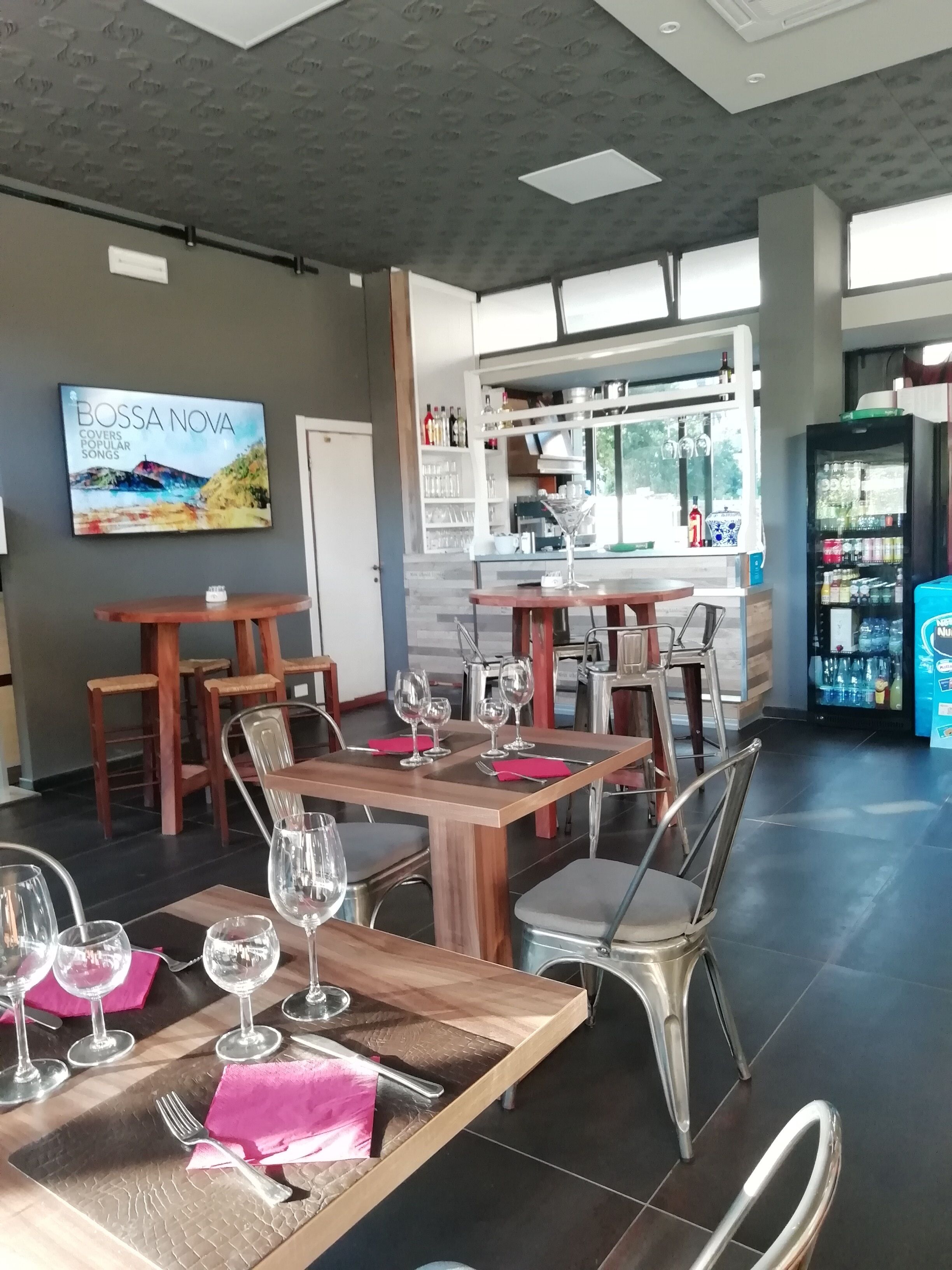 Um restaurante com mesas e cadeiras de madeira, copos de vinho e um bar com prateleiras de garrafas.