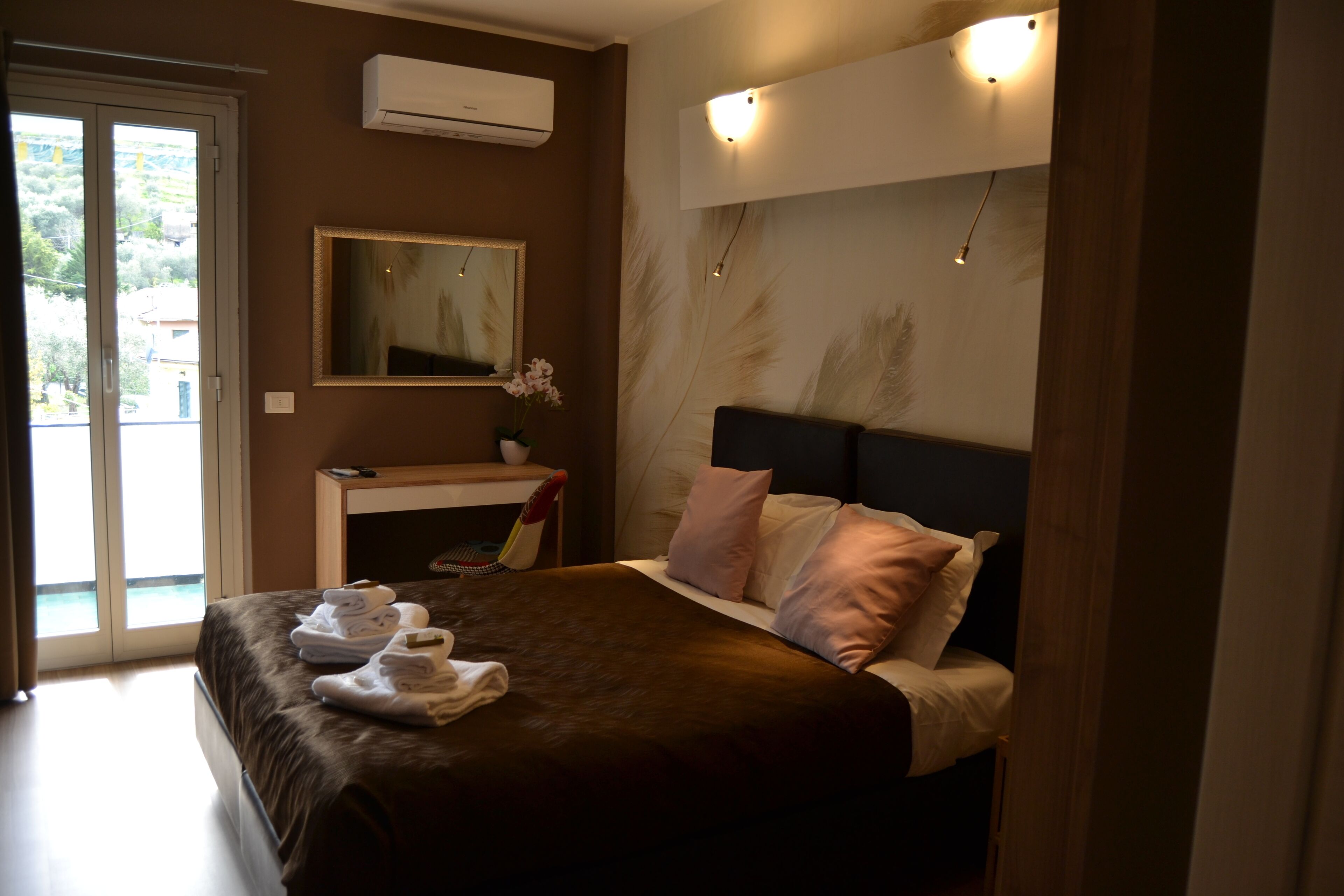 Quarto com cama, escrivaninha, cadeira e uma janela grande.