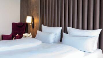 Quarto de hotel com uma cama grande, uma cadeira vermelha e um candeeiro fixado na parede.