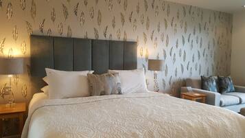 Quarto de hotel com uma cama grande, duas mesas de cabeceira, um sofá e um papel de parede estampado.