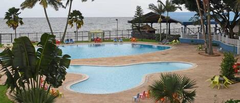 Área de piscina com vista para o mar, cercada por palmeiras e espreguiçadeiras.