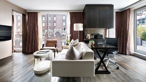Quarto de hotel moderno com sofá, mesa de centro redonda, escrivaninha com cadeira, TV de tela plana na parede e uma grande janela com vista para a cidade.