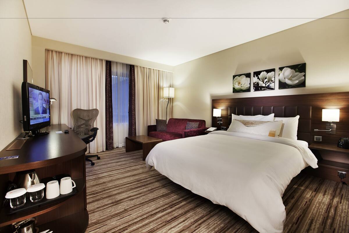 Quarto de hotel com uma cama grande, uma mesa com computador, uma cadeira, um sofá e uma televisão.