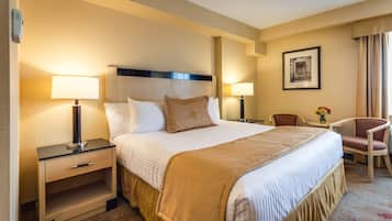 Quarto de hotel com cama grande, duas mesas de cabeceira, uma cadeira e uma pequena mesa com um vaso de flores.