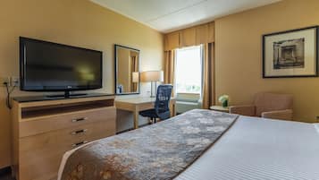 Quarto de hotel com cama, escrivaninha, televisão, cadeira e quadro na parede.
