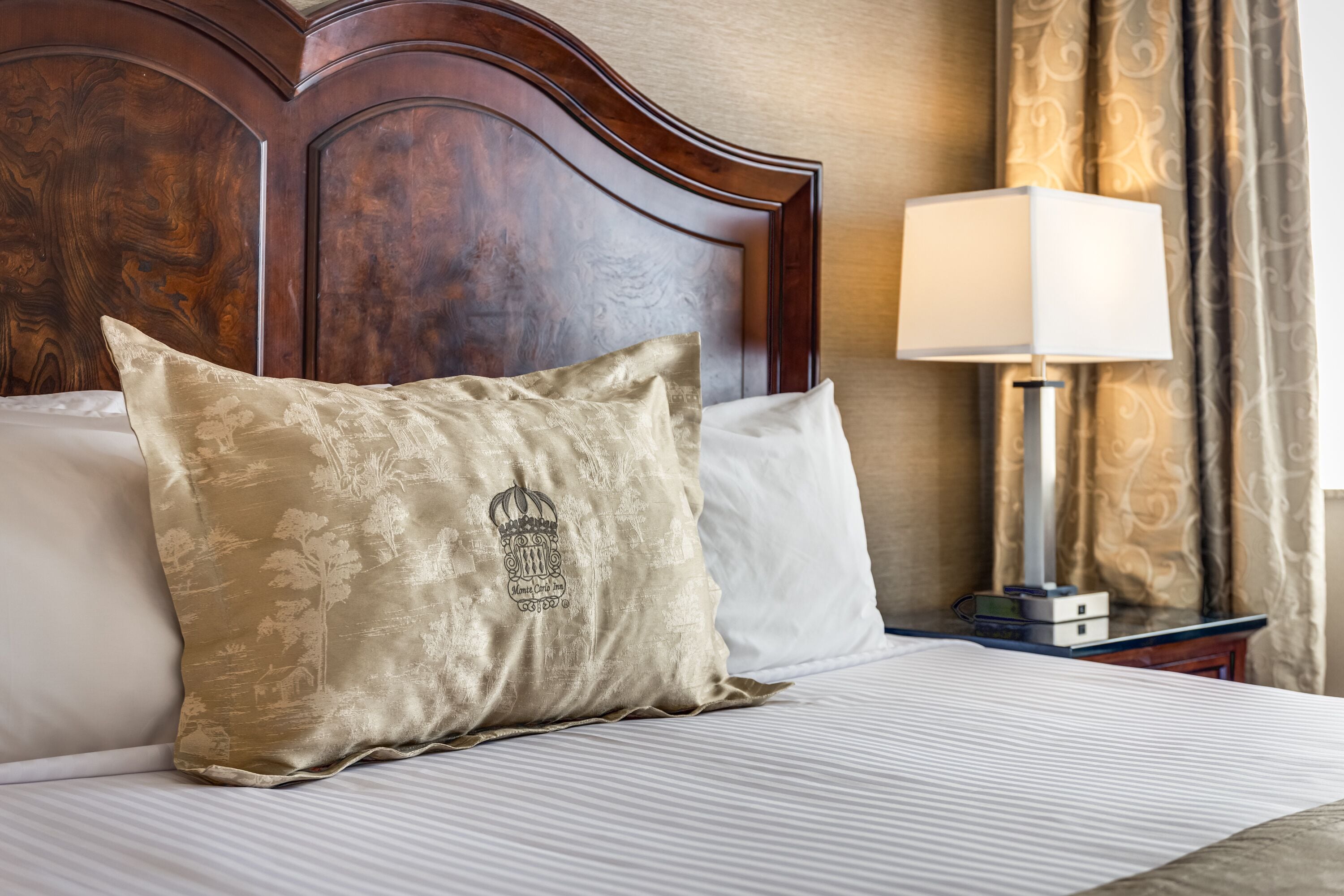 Uma cama bem arrumada com travesseiro decorativo, abajur e cabeceira de madeira.