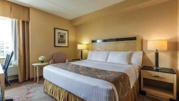 Quarto de hotel com cama, mesas de cabeceira, uma cadeira, abajur e um quadro na parede.