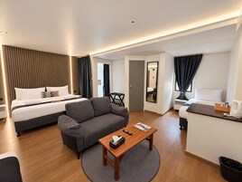 Quarto de hotel moderno com cama, sofá, mesa de centro e um espaço de trabalho.