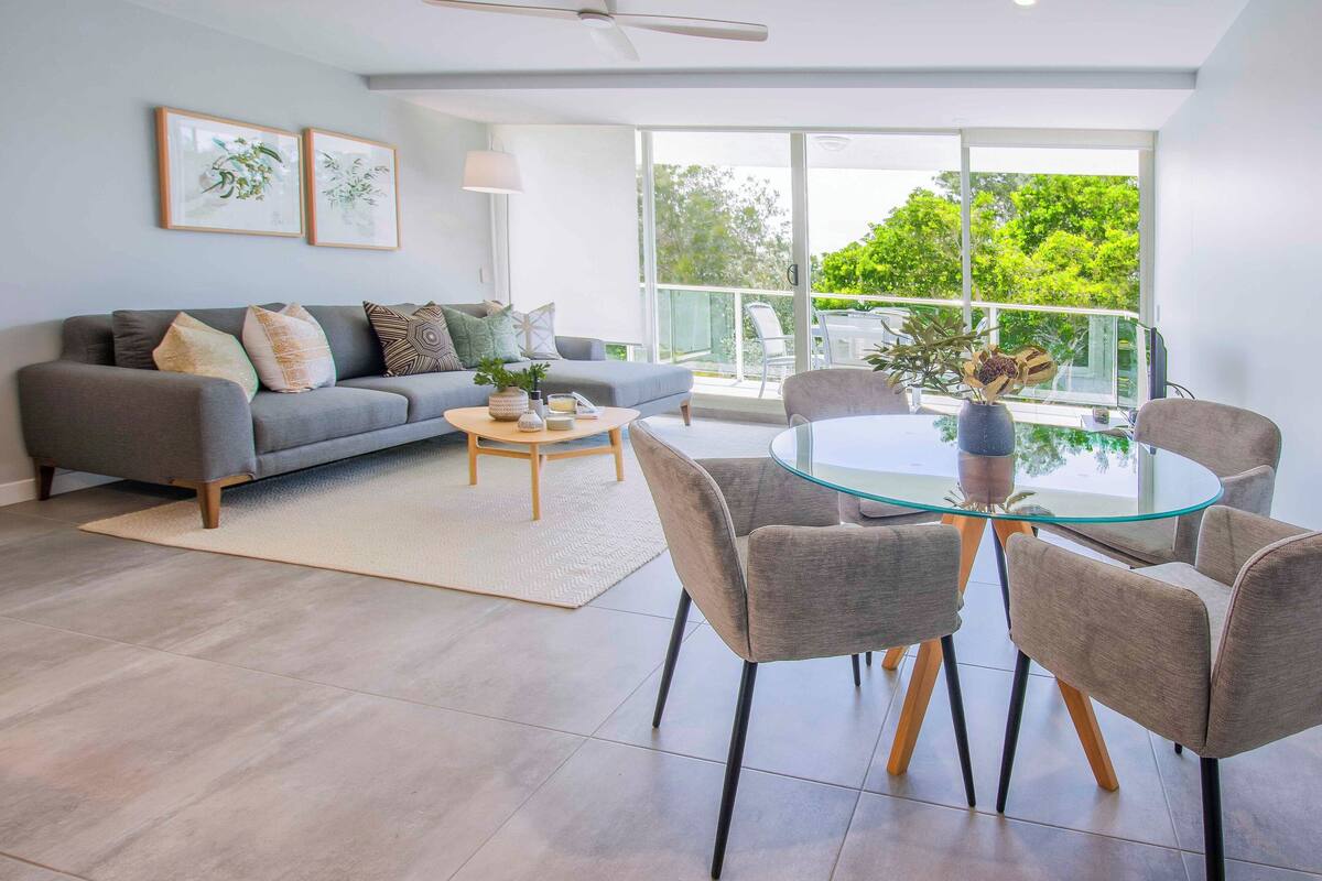 Uma sala de estar moderna com um sofá cinzento, uma mesa de centro de vidro e cadeiras cinzentas.