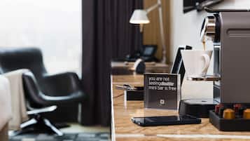 Quarto de hotel com cafeteira, placa indicando minibar grátis, smartphone e uma cadeira.