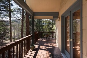 Um deck de madeira com mesa e cadeiras, com vista para uma área arborizada.