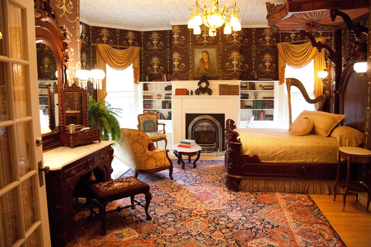 Quarto tradicional com uma cama grande, lareira, estante de livros e mobiliário decorado.