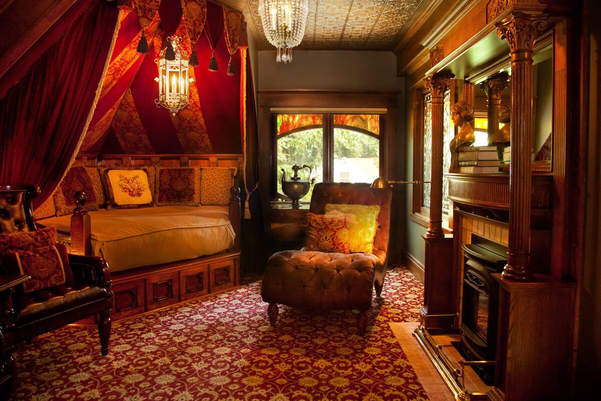 Quarto com cama, poltrona de leitura, lareira e uma janela grande.