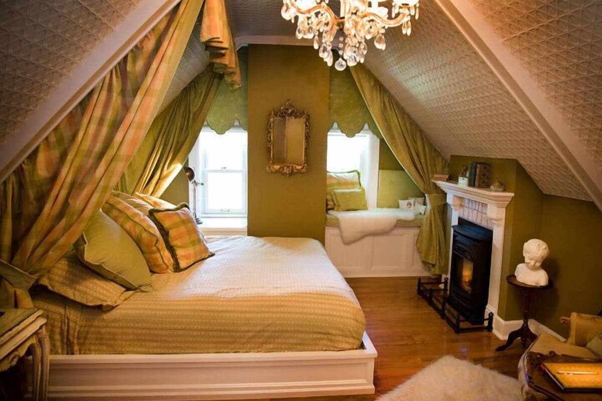 Um quarto de sótão aconchegante, com uma cama grande, uma lareira e uma janela com cortinas.