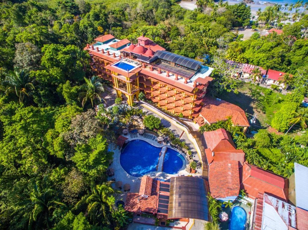 Resort com uma grande piscina, área coberta com telhado e vegetação exuberante ao redor.