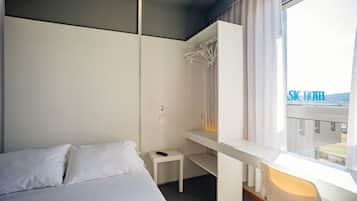 Quarto de hotel moderno com cama, escrivaninha e janela com vista para um edifício identificado como