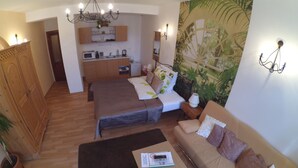 Quarto com cama, sofá, escrivaninha, espelho, lustre, cozinha e uma planta grande.