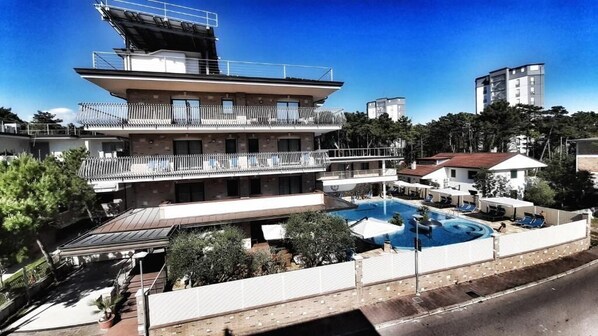 Um edifício com várias andares, varandas, piscina e área externa coberta.