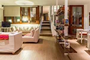 Uma sala de estar moderna com um sofá, uma mesa de centro e uma televisão. Há uma escada que leva a outro andar.